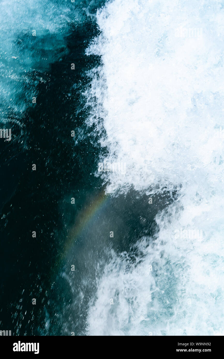 the small rainbow appear behind the boat in dark blue raging water ...