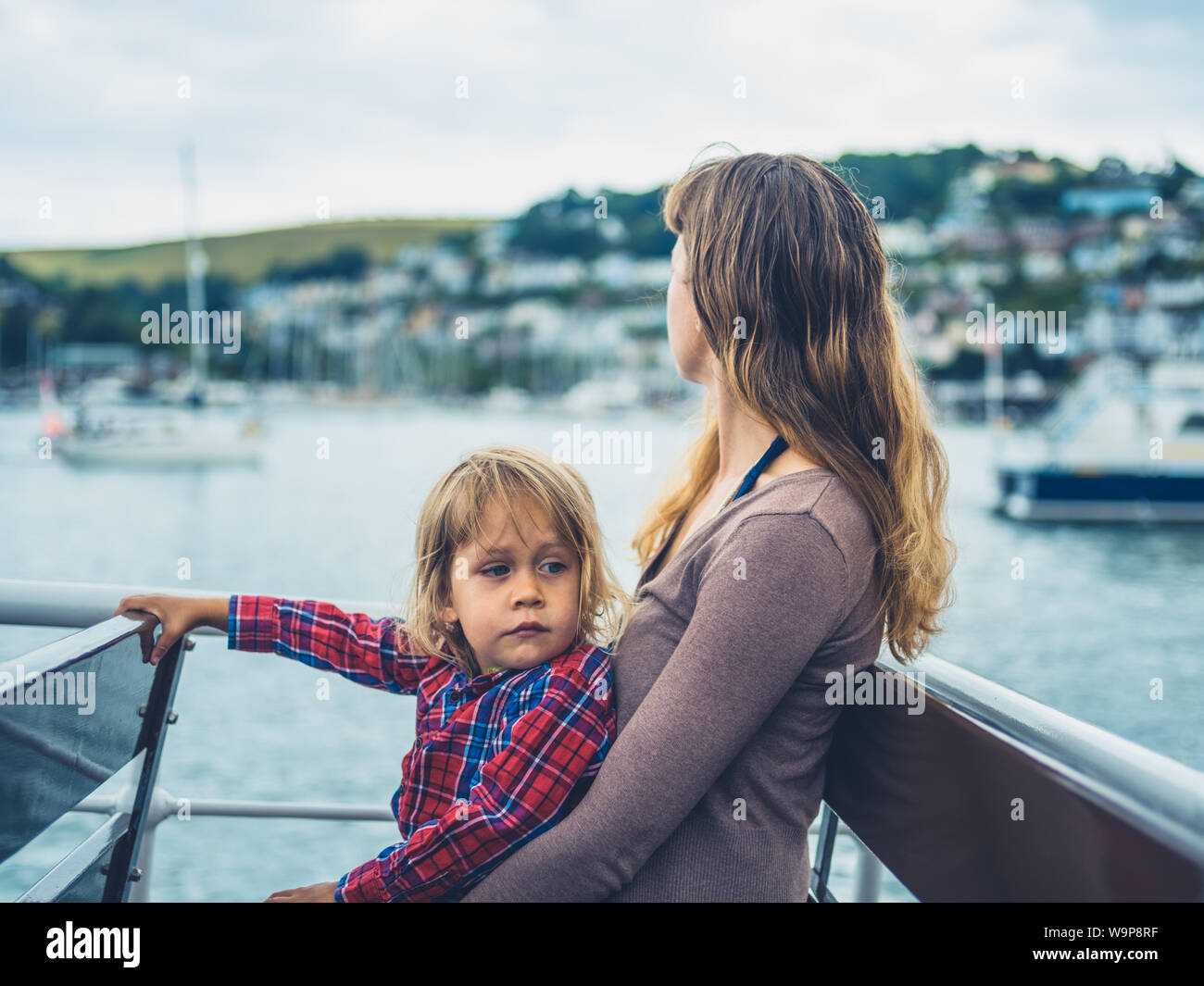 A young mother and her toddler are sitting on a boat in the harbor ...