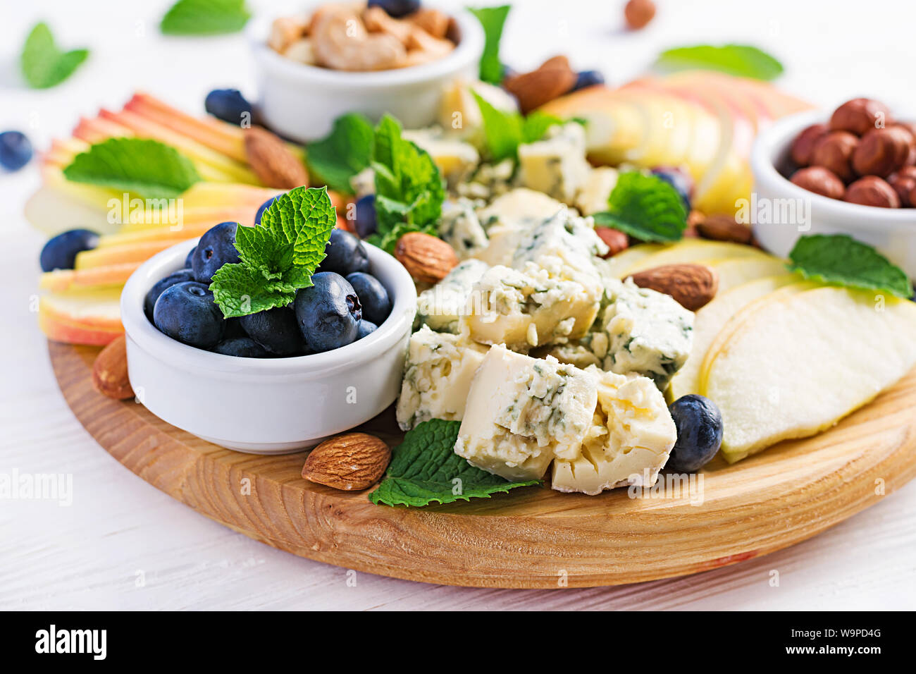 Cheese platter with assorted cheeses, blueberry, apples, nuts on white ...