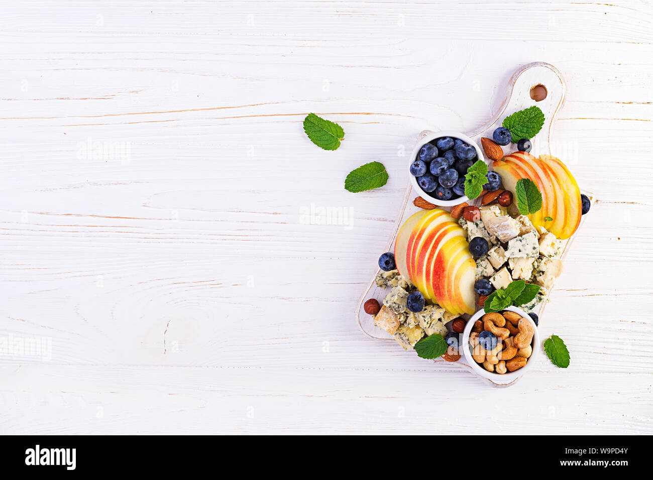 Cheese platter with assorted cheeses, blueberry, apples, nuts on white ...