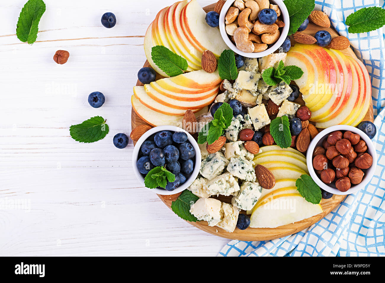 Cheese platter with assorted cheeses, blueberry, apples, nuts on white ...