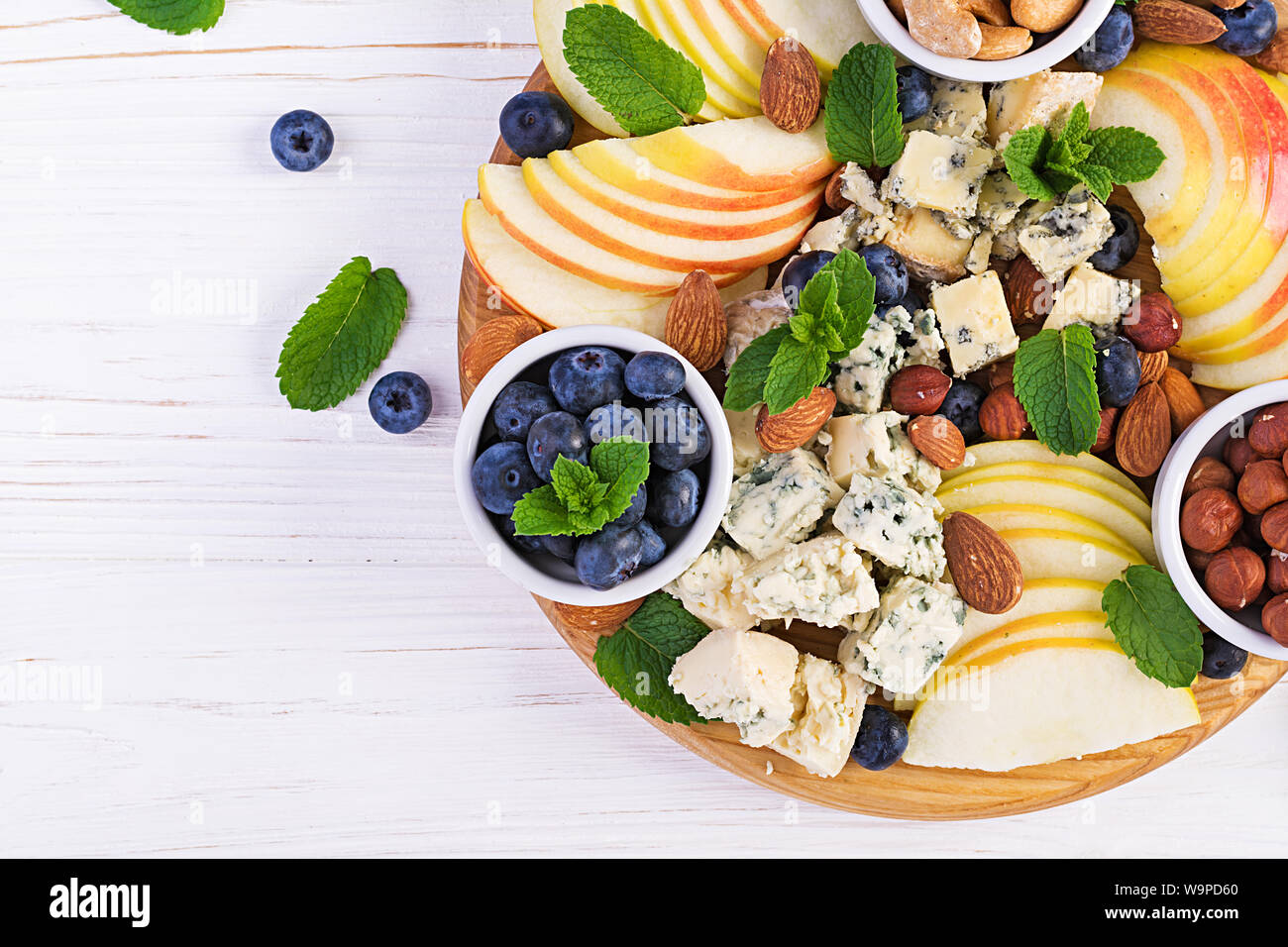 Cheese platter with assorted cheeses, blueberry, apples, nuts on white ...