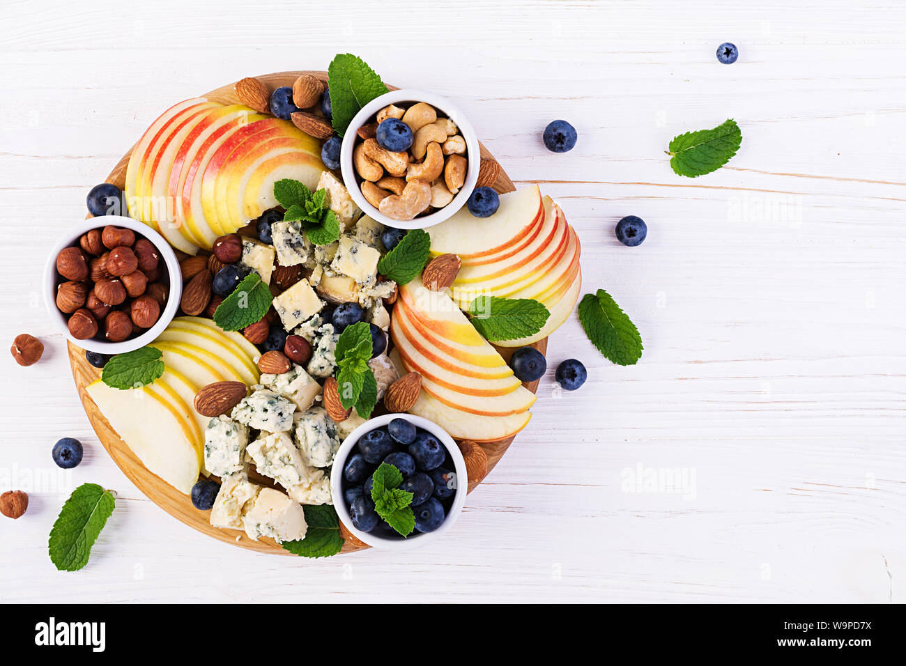 Cheese platter with assorted cheeses, blueberry, apples, nuts on white ...