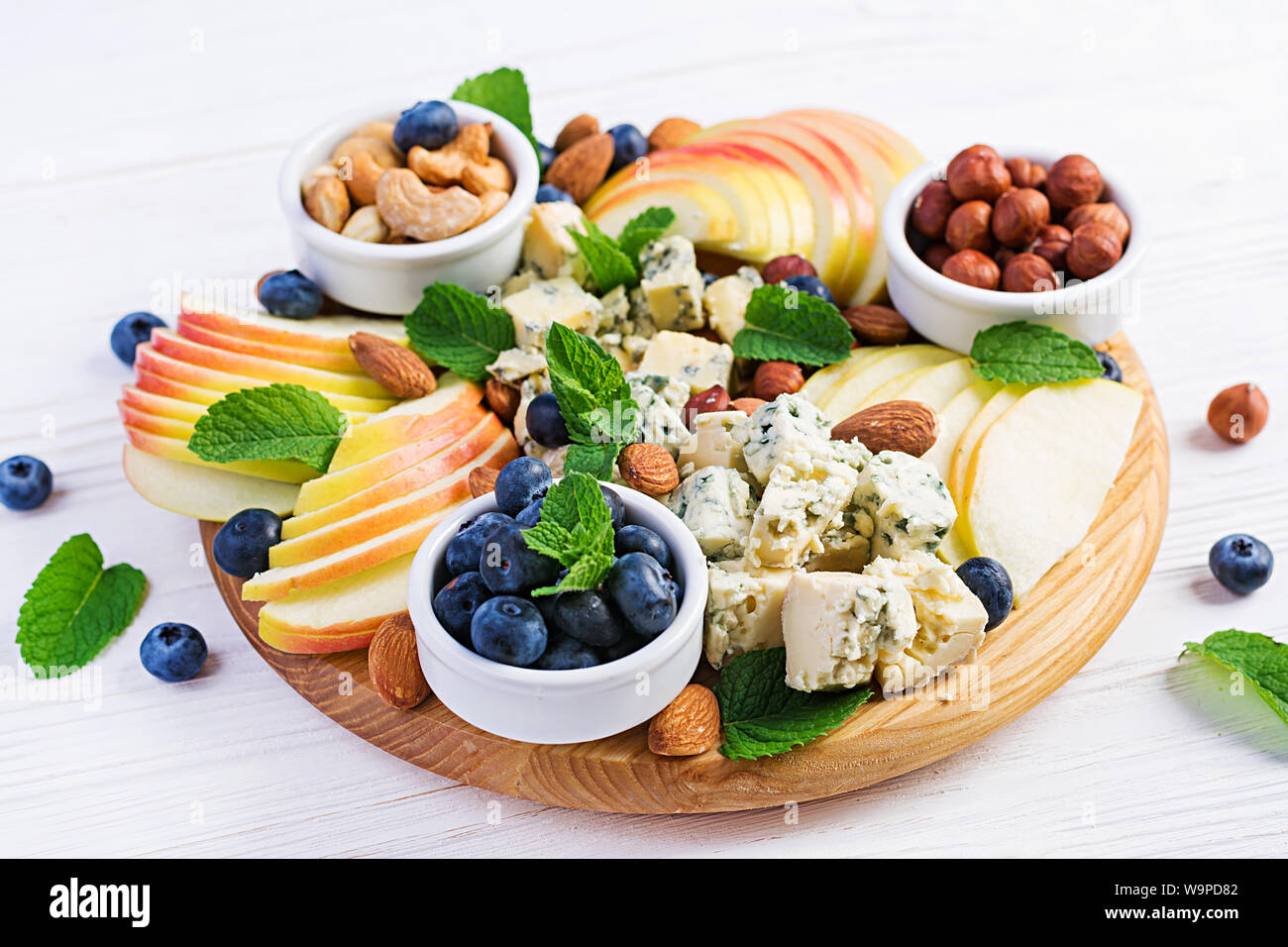 Cheese platter with assorted cheeses, blueberry, apples, nuts on white ...