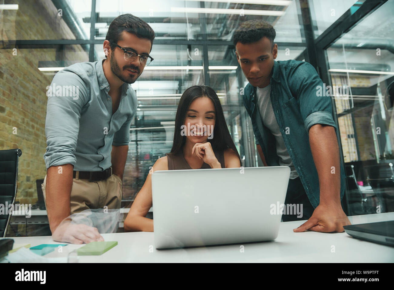 Great results! Group of three young employees looking at screen of ...