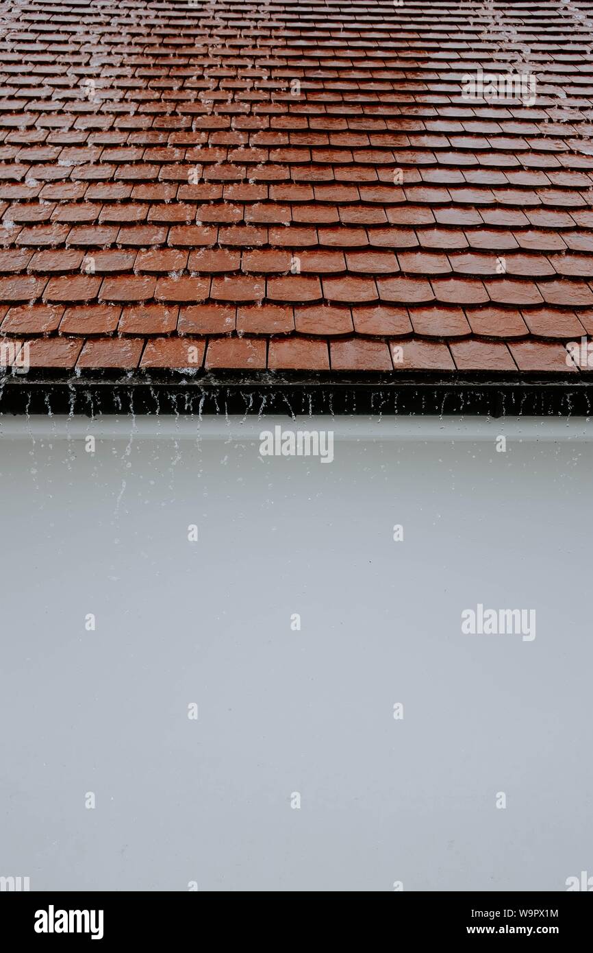 Vertical shot of wet roof tiles with water flowing down during a rain ...