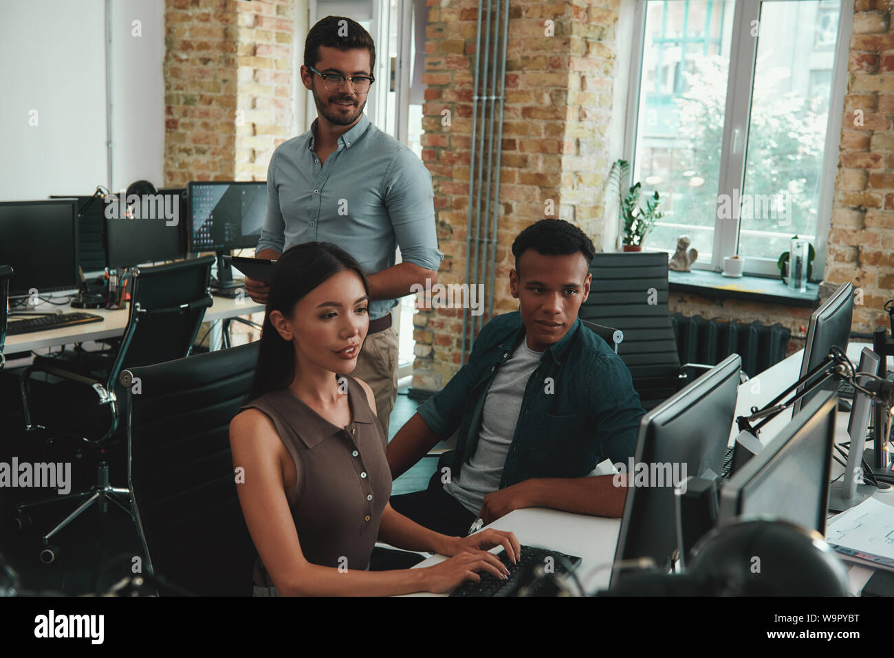 Focused on work. Group of young employees looking at computer monitor ...