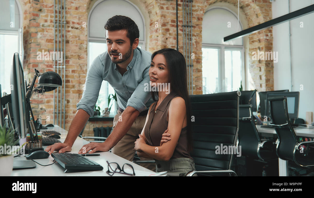 Look here Two young colleagues in casual wear looking at computer ...