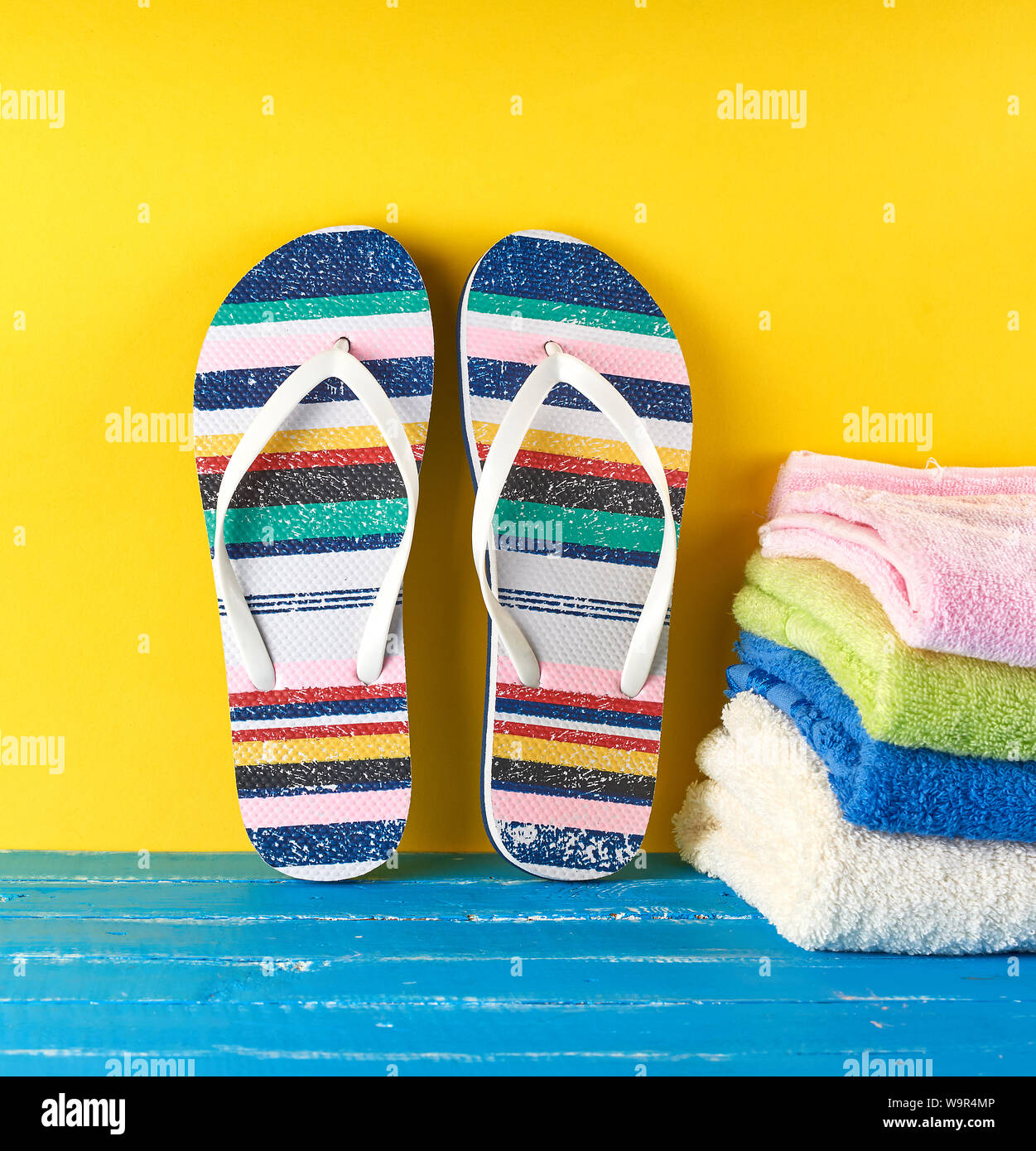 pair of female beach slippers and a towels on a blue yellow background ...