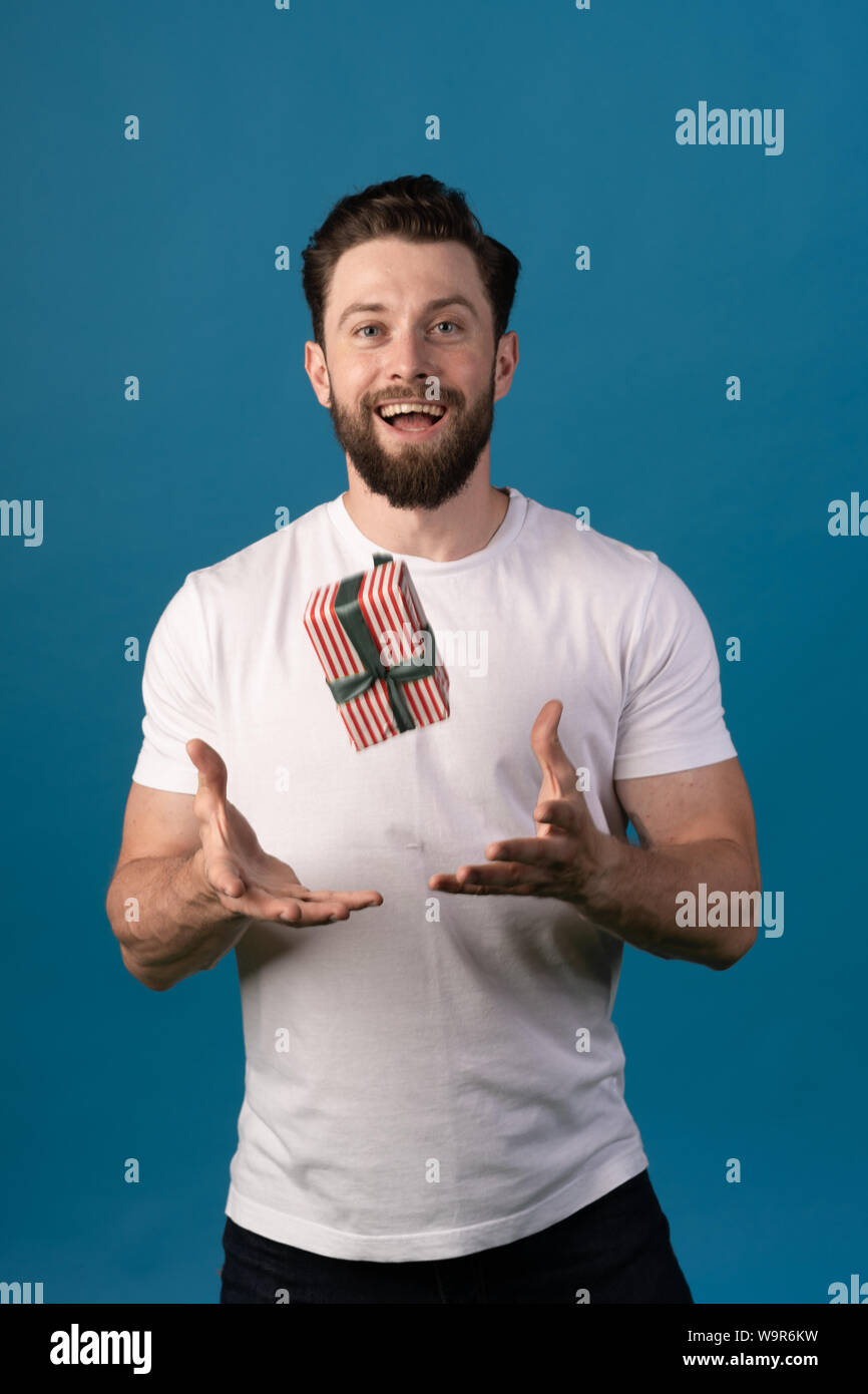 Young man looking casual in surprise throwing big red present gift box ...