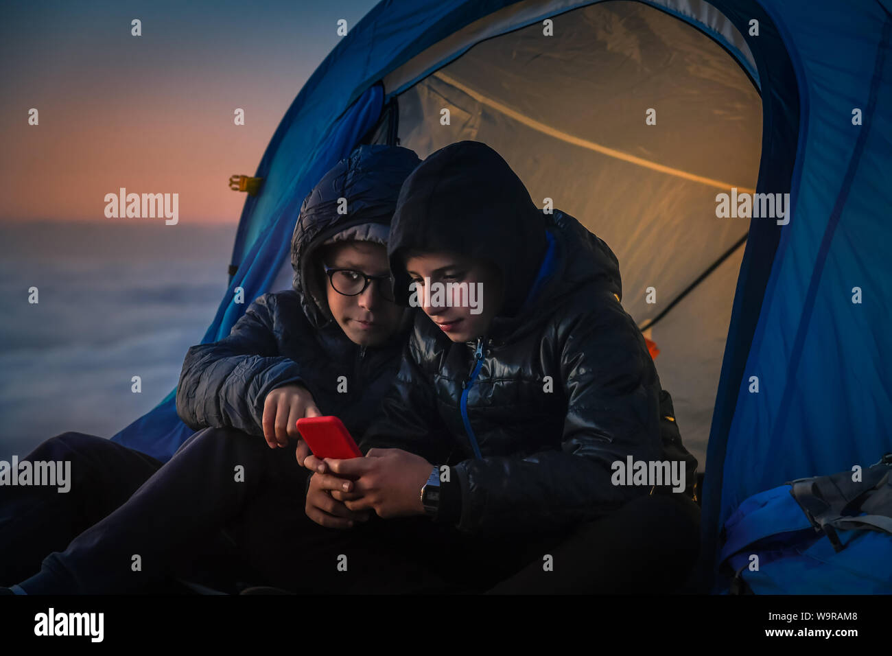 Two boys playing with smartphone sitting in a camping tent. Couple of ...