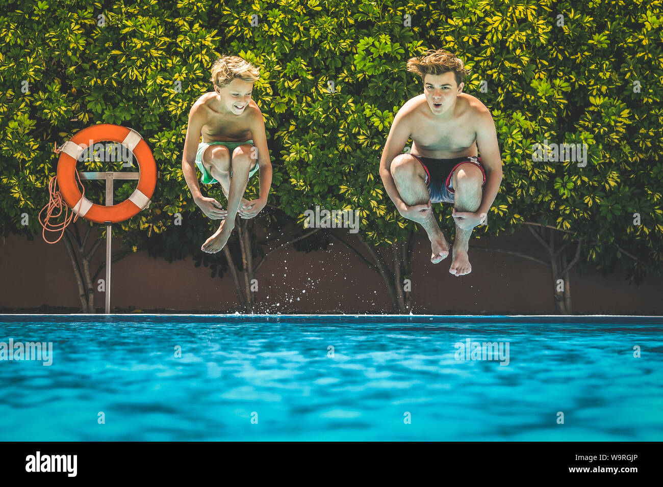 Two young boys having fun diving into the swimming pool.View from the ...