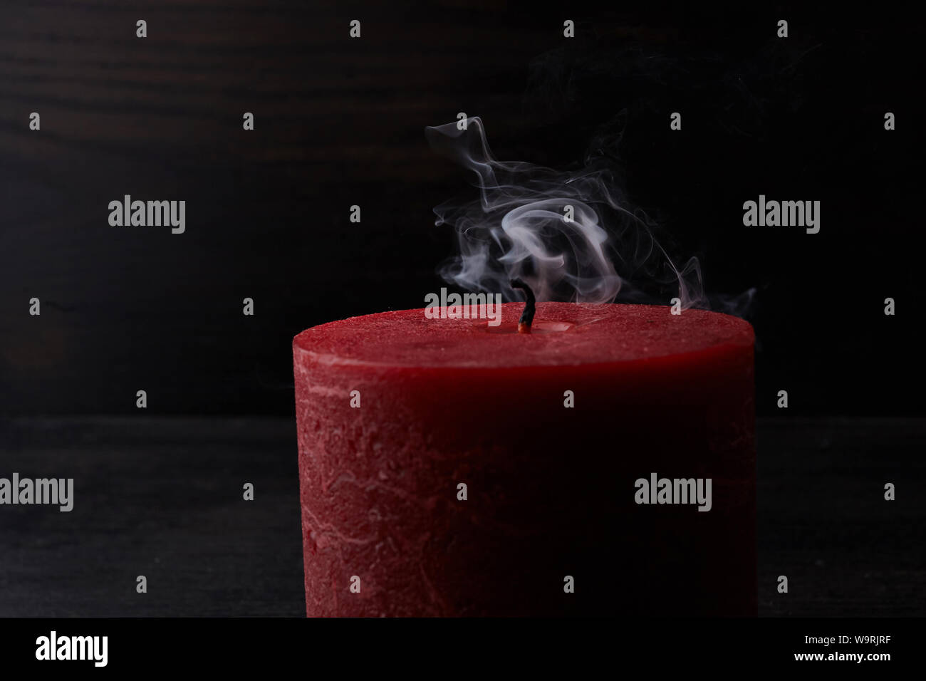 Red extinguished candle with smoke trailing off the wick on dark ...