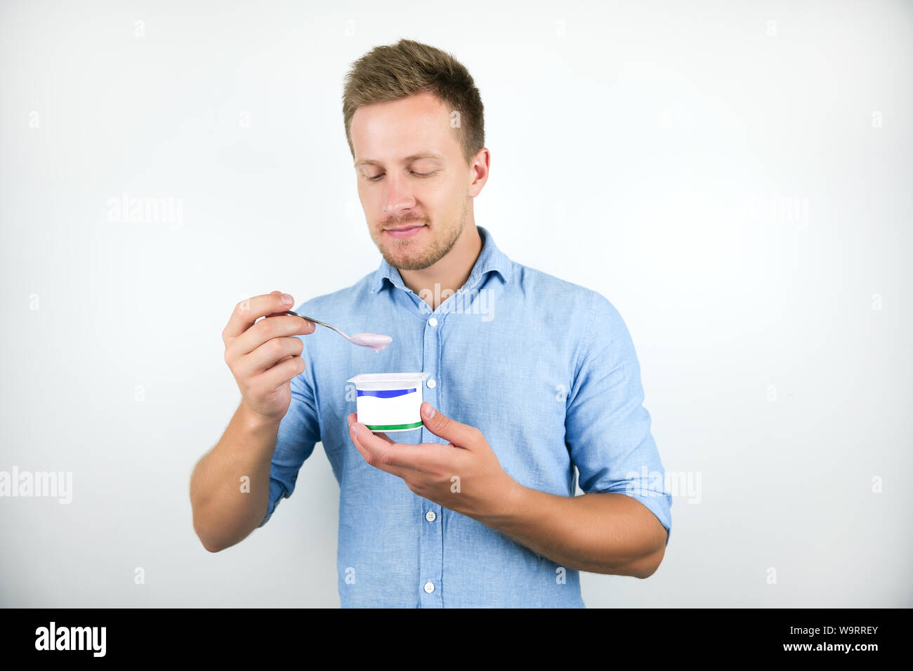 young handsome man eats yogurt with spoon on isolated white background ...