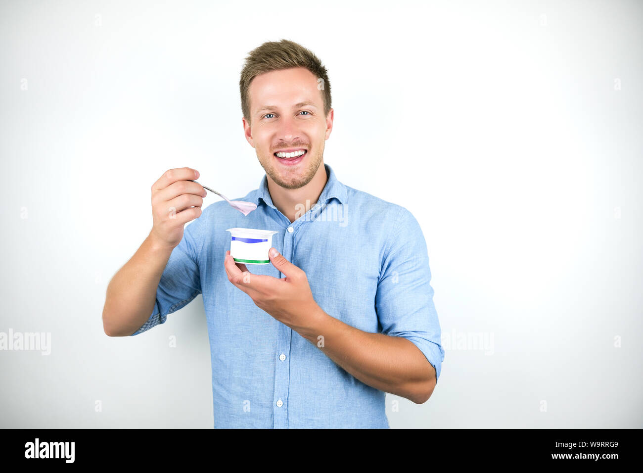 young handsome man eats yogurt with spoon smiling on isolated white ...