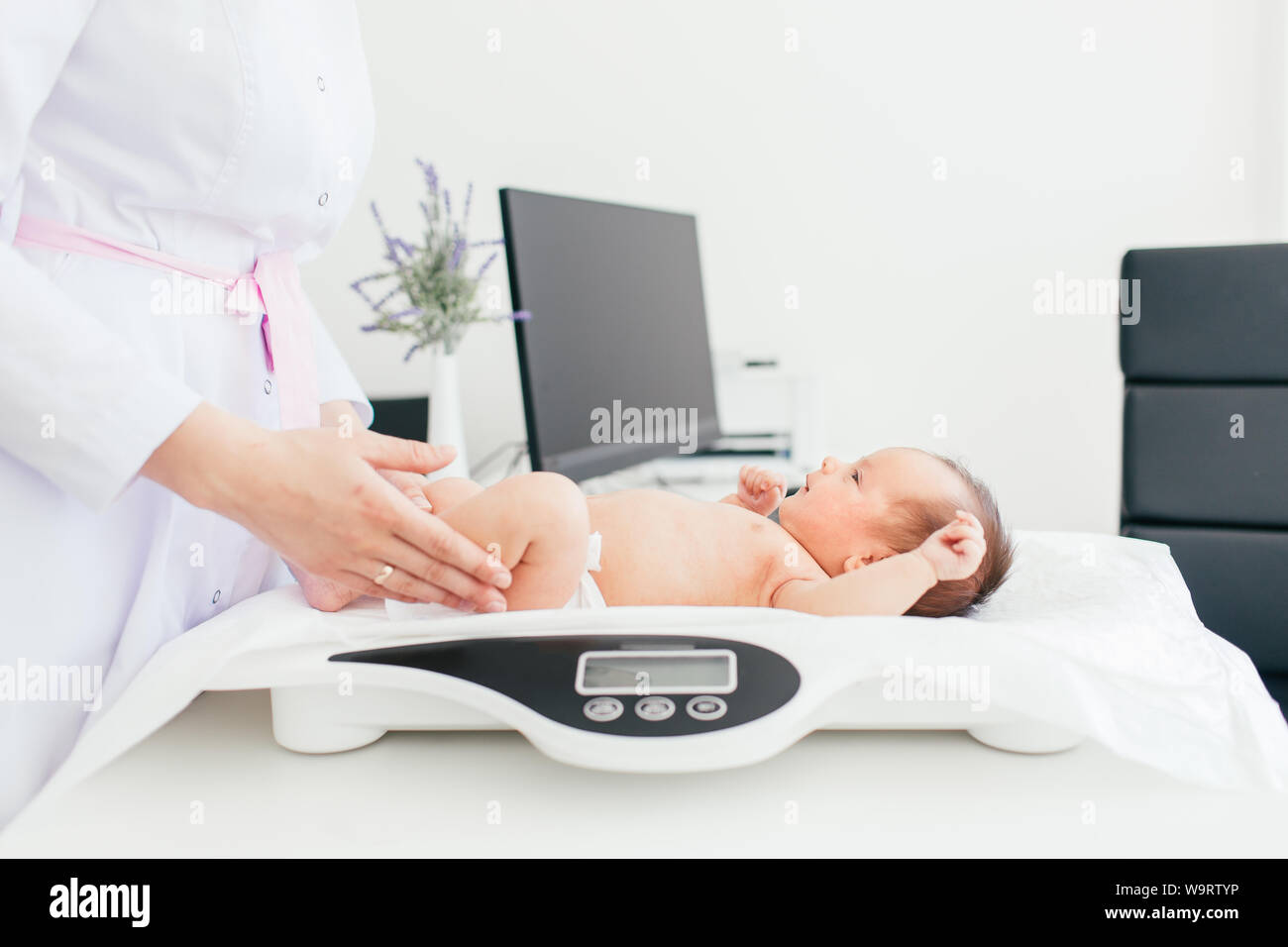 Cute little baby lying on scales, medical checkup in clinic, copy space ...