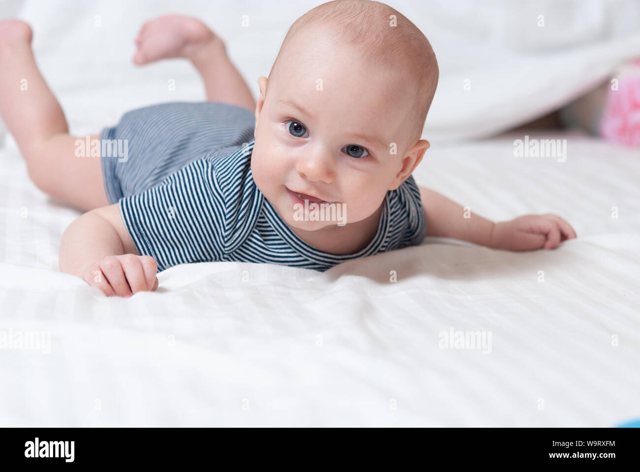 Happy cute four month old baby lying on his stomach on a bed in his ...