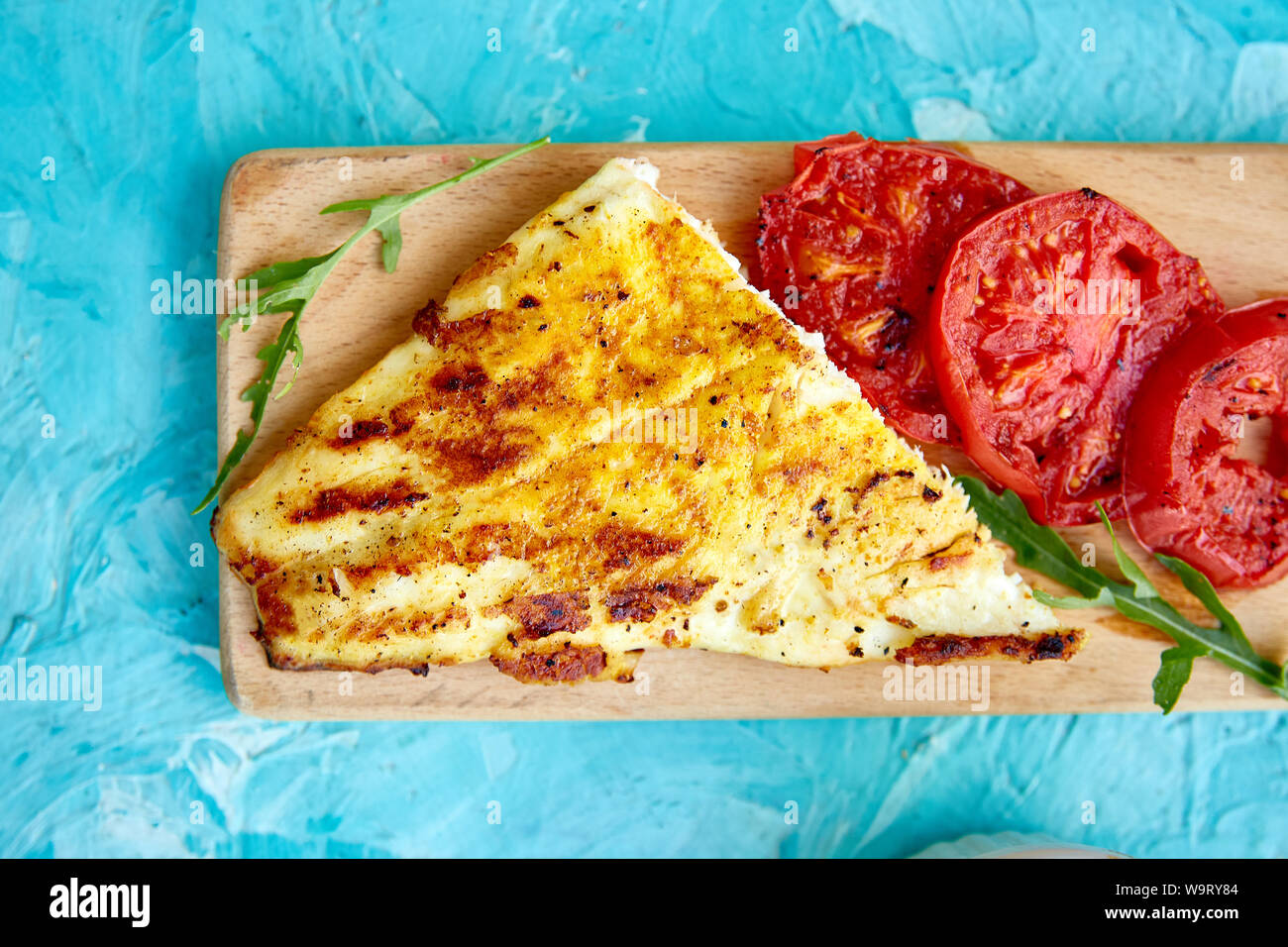 Grilled pike fillet with tomatoes on wooden board on blue background ...