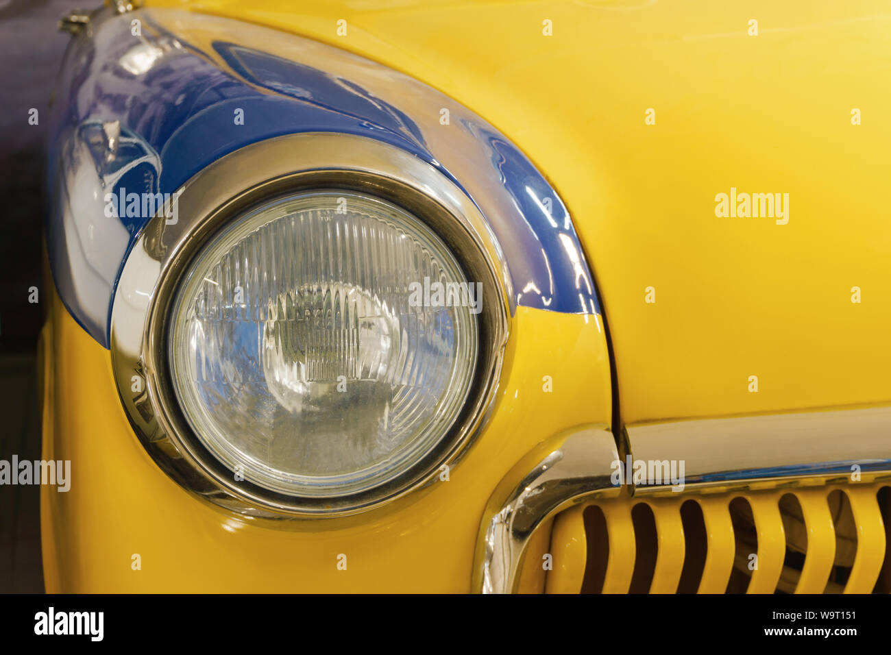 detail of the front part of a blue-yellow vintage car, headlight and ...