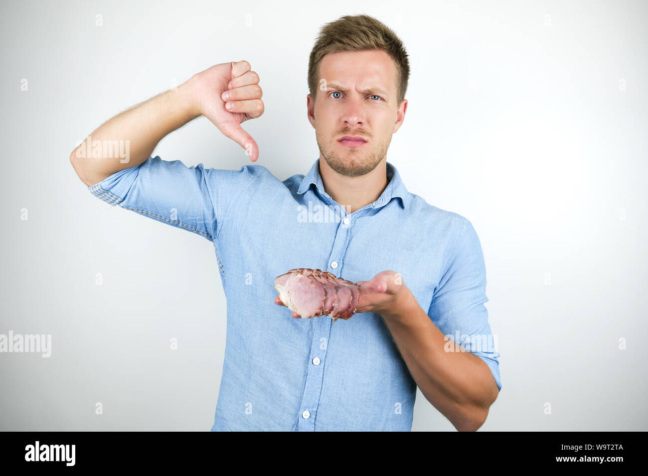young handsome man holding sliced bacon showing dislike sign on ...