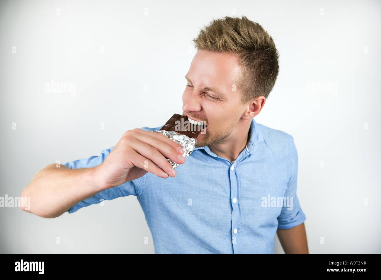 young handsome man biting chocolate bar feeling hungry on isolated ...