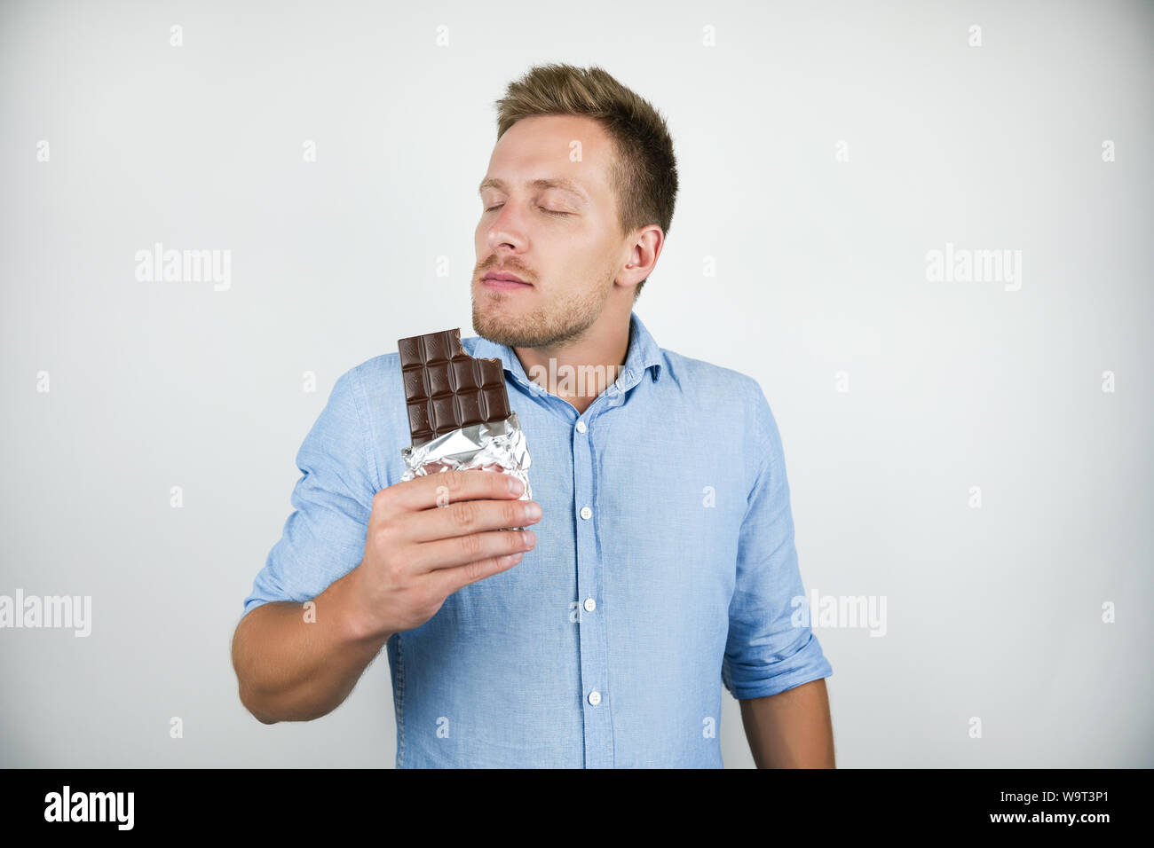 young handsome man holding chocolate bar looking satisfied on isolated ...