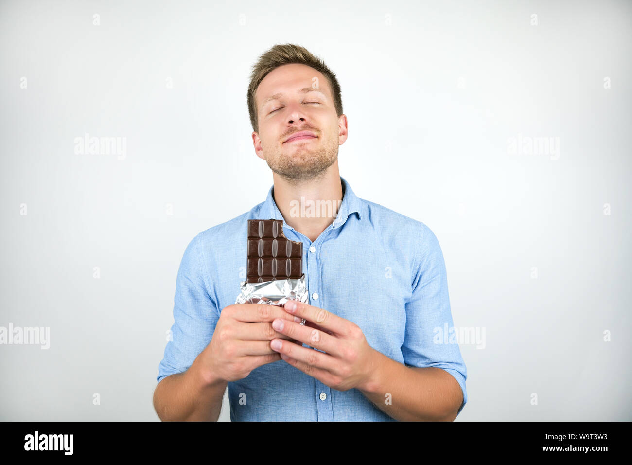 young handsome man holding chocolate bar looking pleased on isolated ...