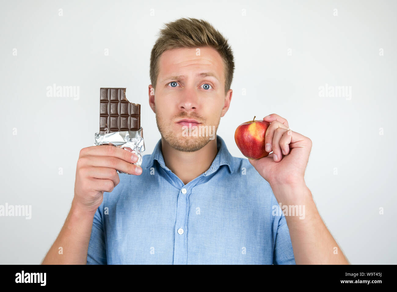 young handsome man holding chocolate bar in one hand and fresh ripe ...
