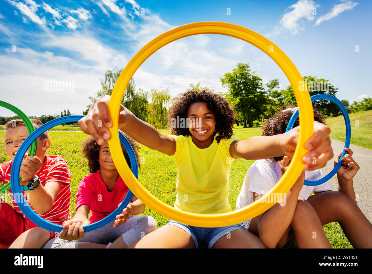 Girl in group of kids look through colorful hoop Stock Photo - Alamy