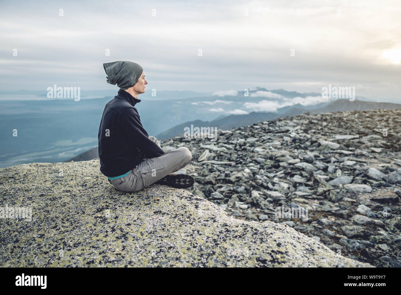 Man hiker sitting in a yoga pose at the peak of the mountain in the ...