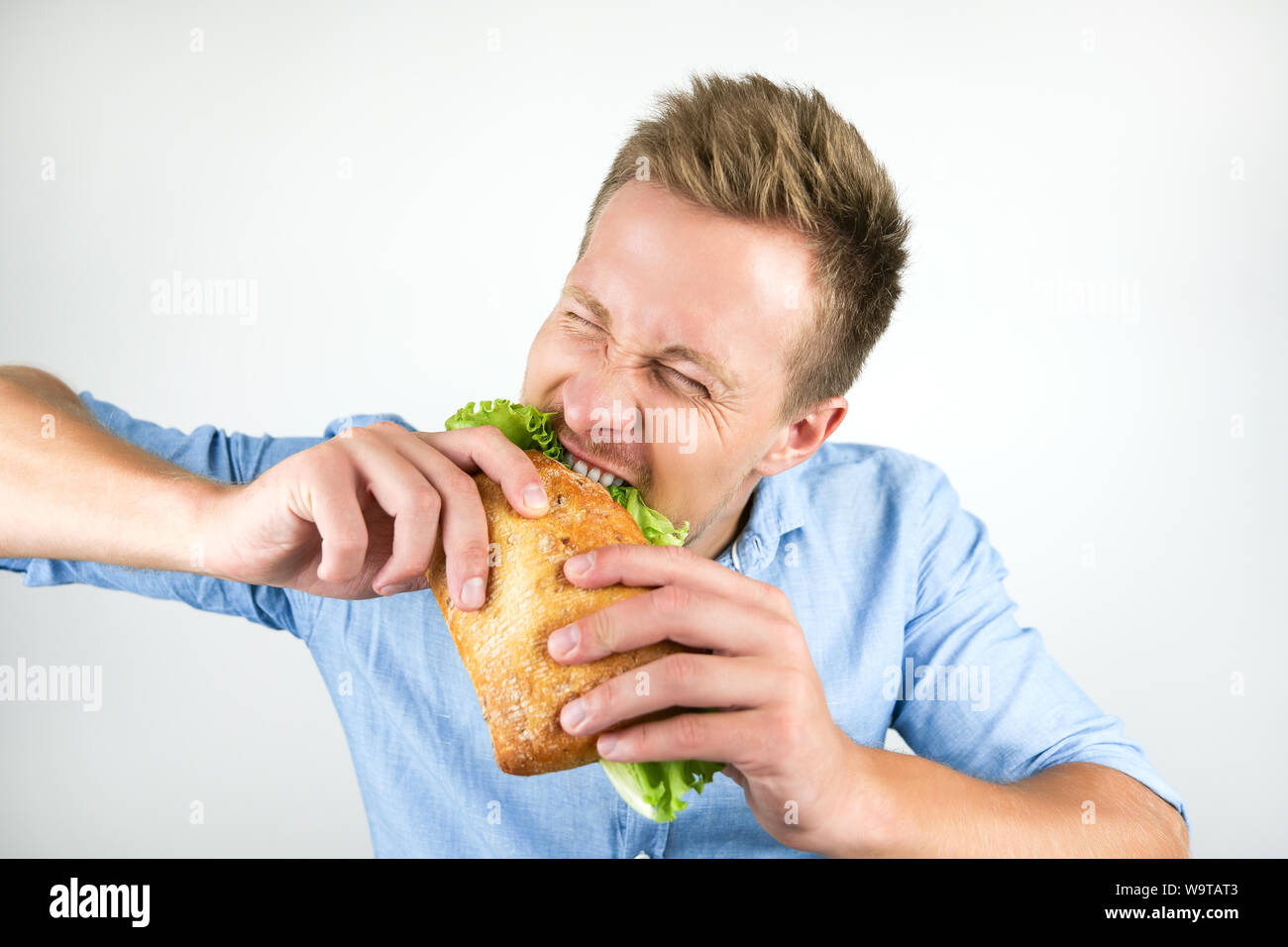 young handsome man biting fresh sandwich with hunger on isolated white ...