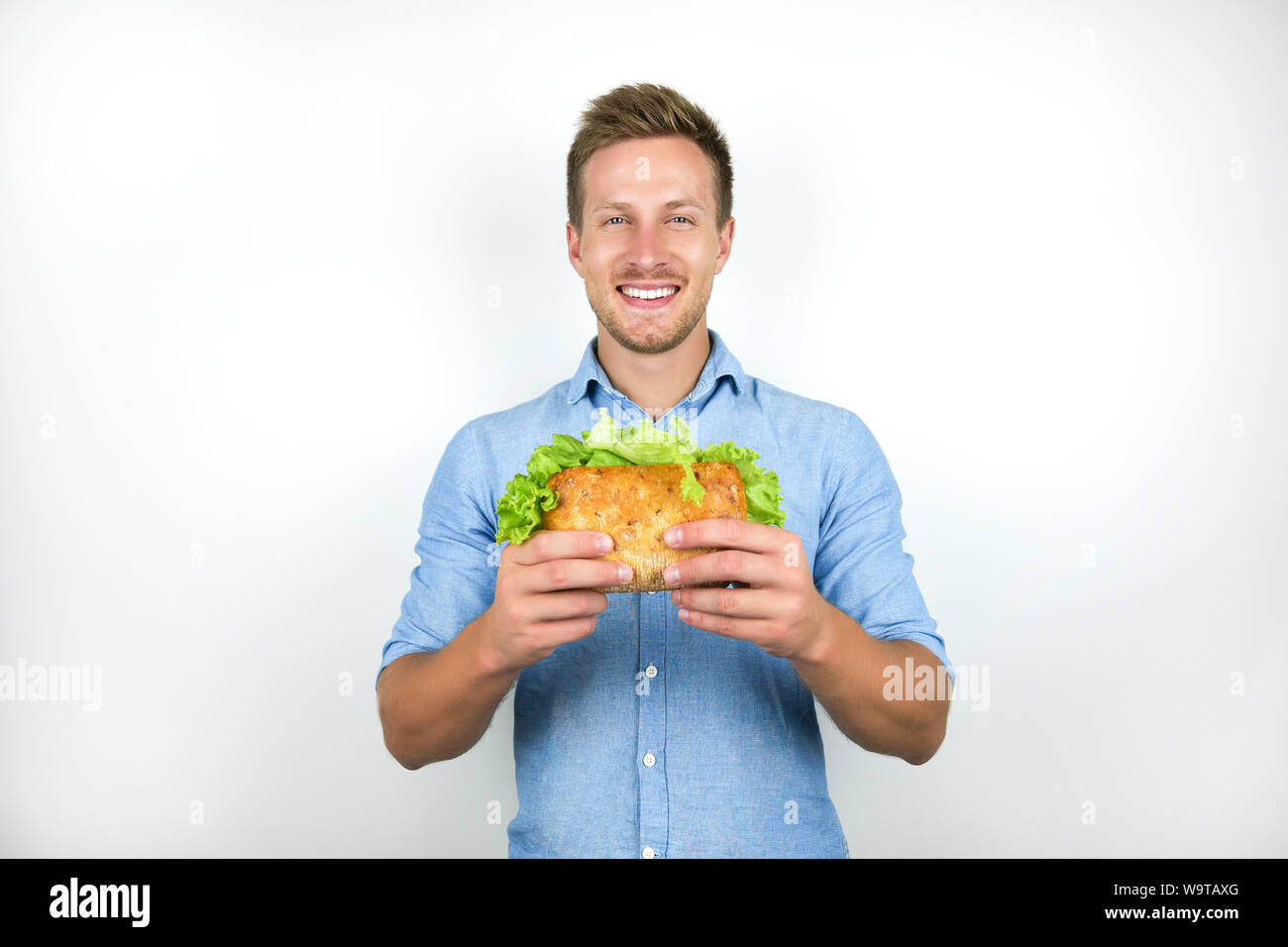 young handsome hungry man looks hungry and happy holding fresh sandwich ...