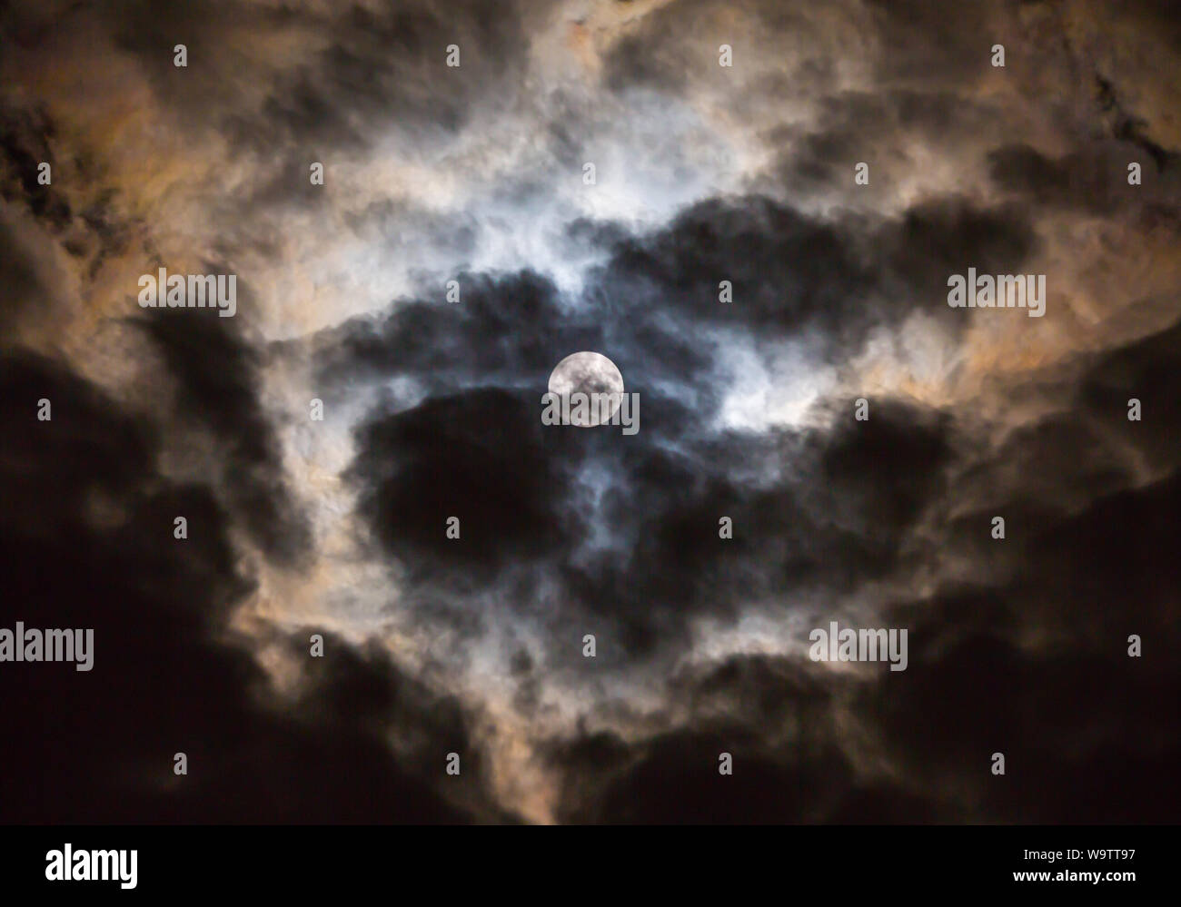 The glow of a full moon dramatically lights clouds in a night sky Stock ...