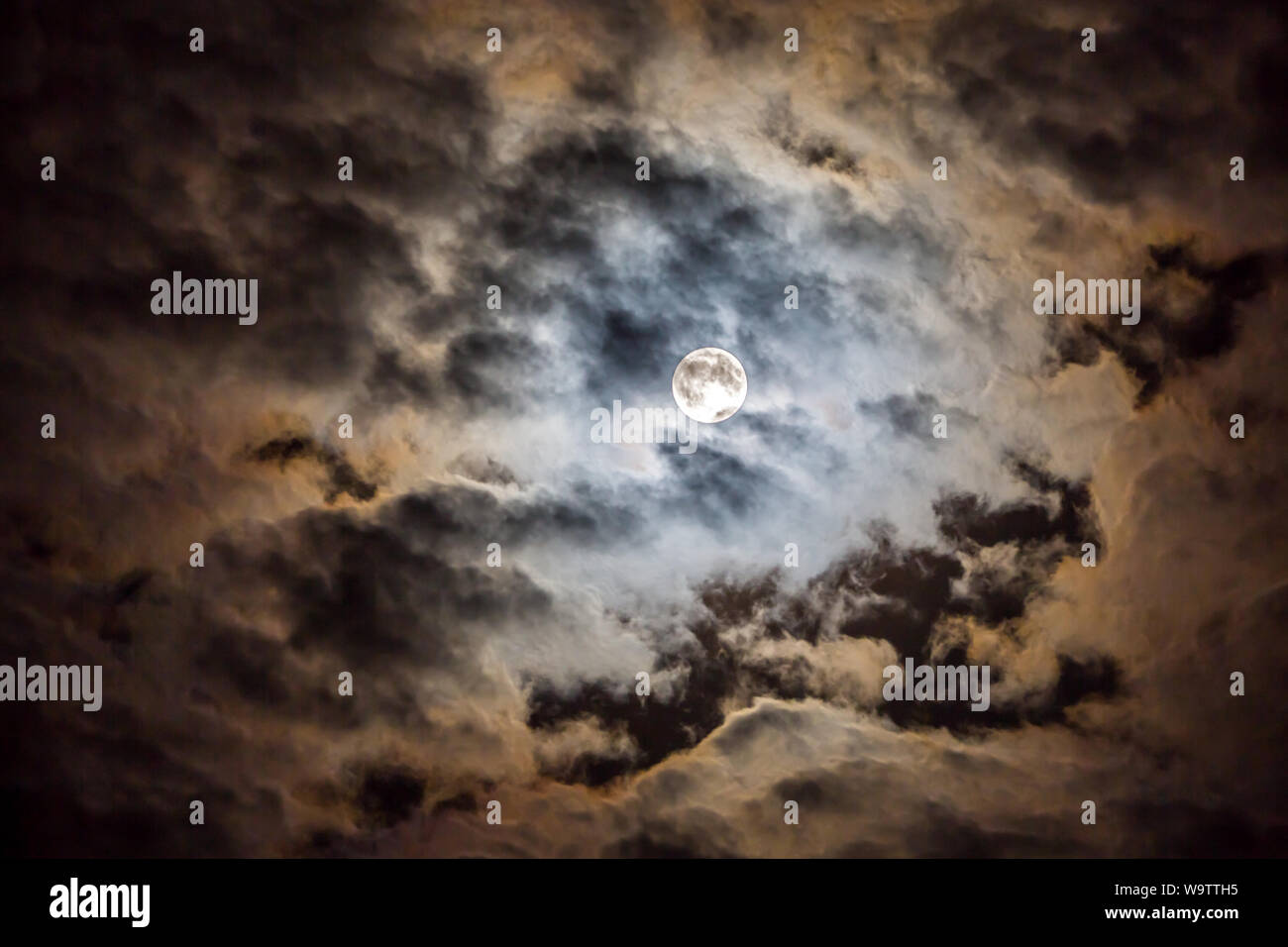 The glow of a full moon dramatically lights clouds in a night sky Stock ...