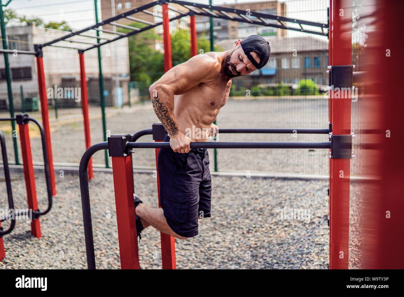 Strong muscular man doing push-ups on uneven bars in outdoor street gym ...