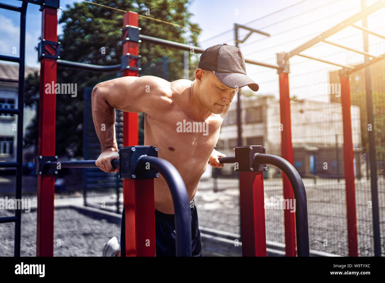 Strong muscular man doing push-ups on uneven bars in outdoor street gym ...
