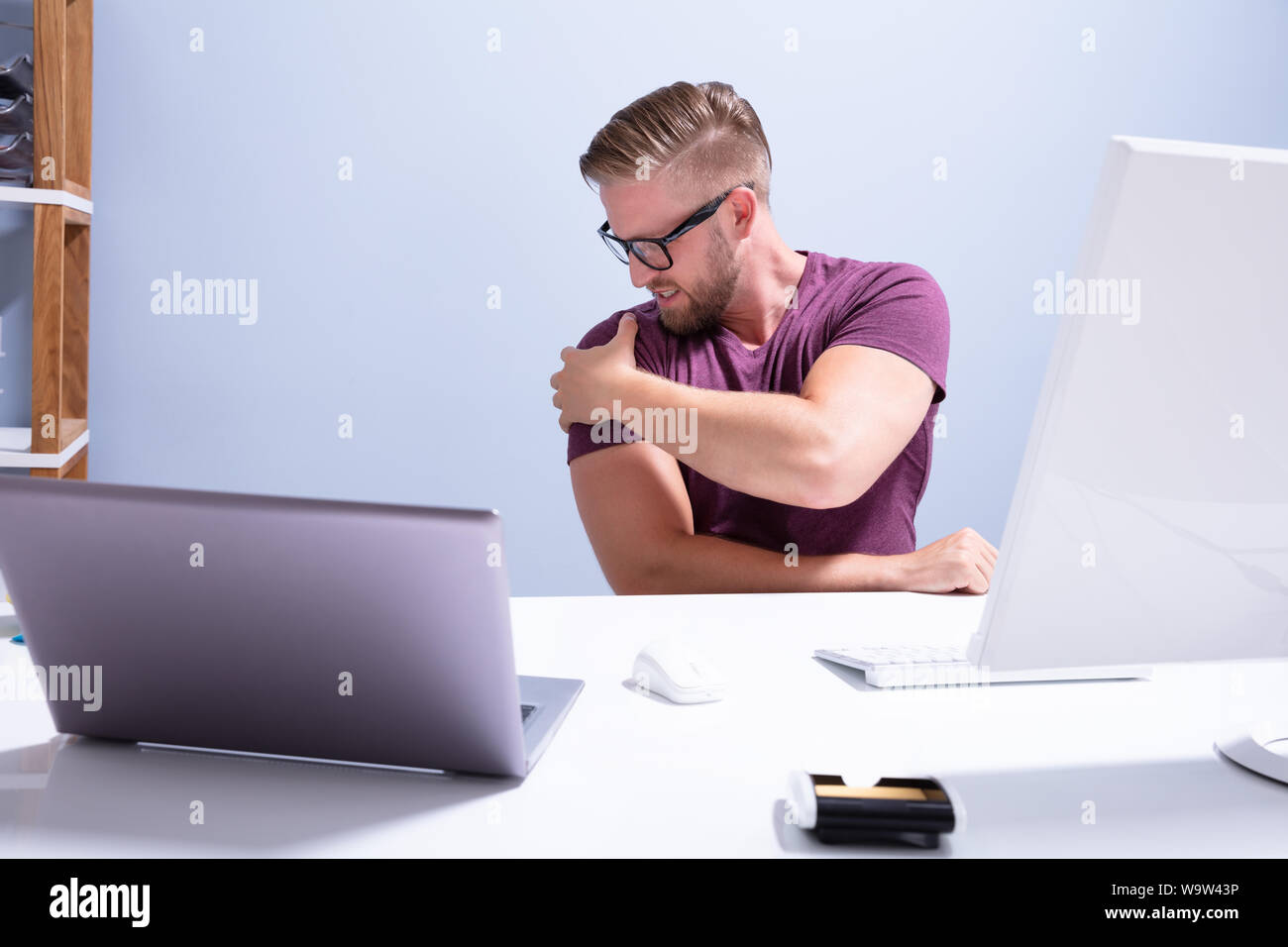 Side View Of A Young Man Sitting On Chair Suffering From Shoulder Pain ...