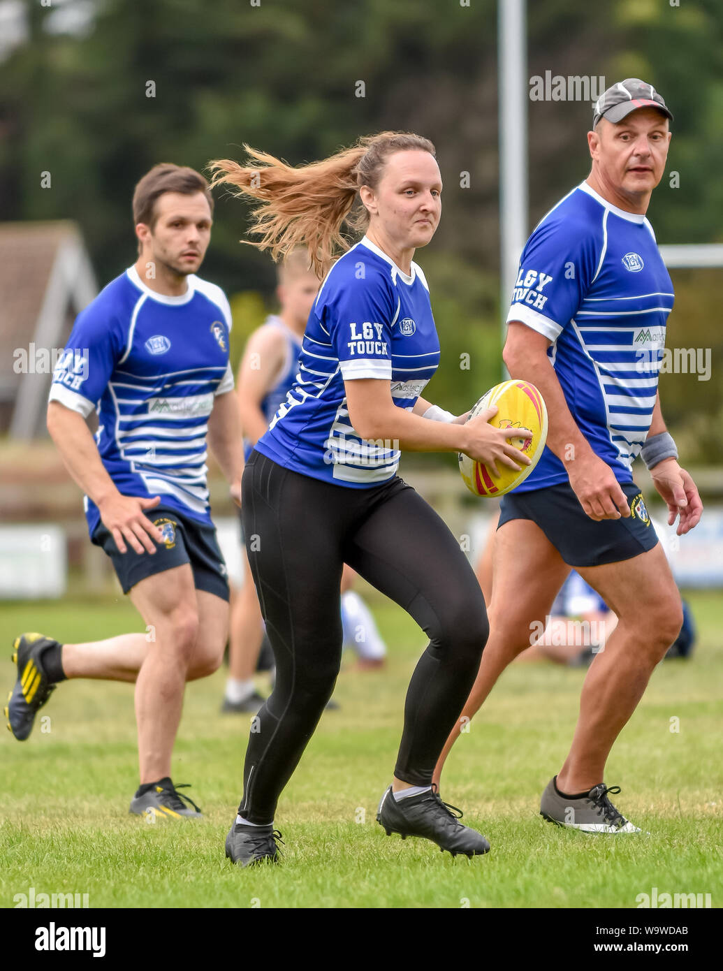 Woman player runs with ball in hand while male players watch at amateur ...