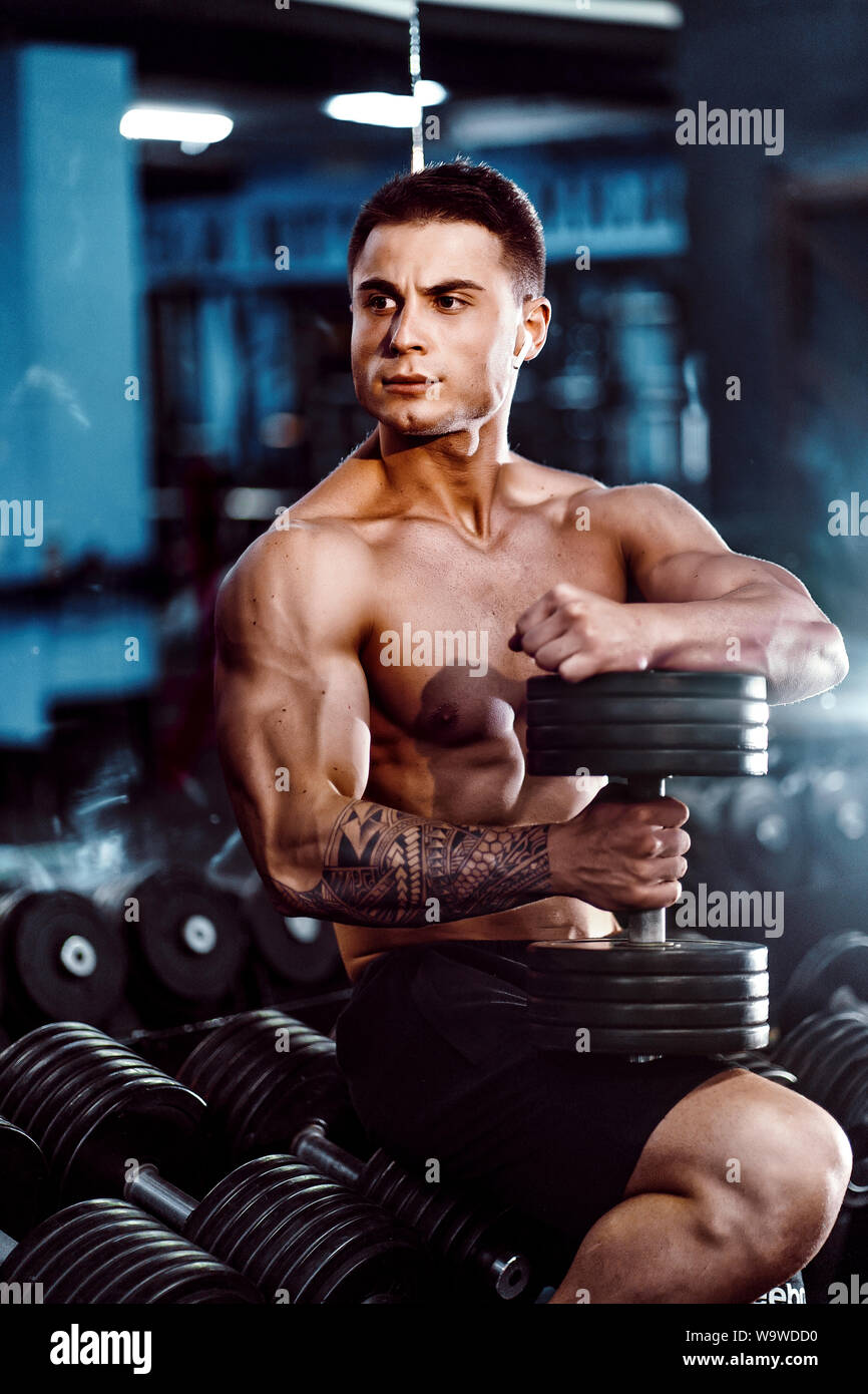 young adult man handsome athlete working out in gym, sitting on a bench ...