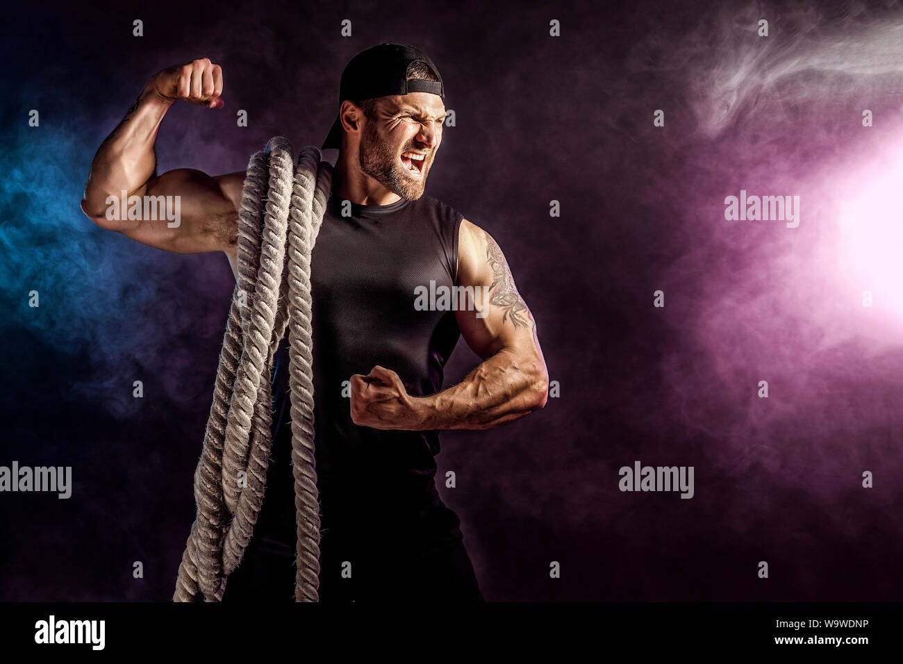 Bearded athletic looking bodybulder holding battle rope on dark studio ...