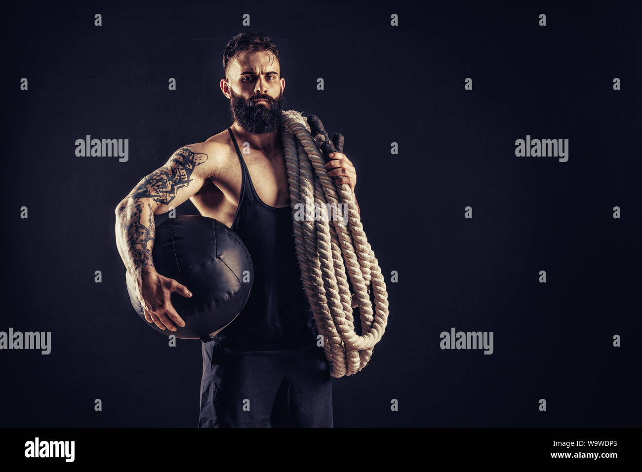Bearded athletic looking bodybulder holding battle rope on dark studio ...