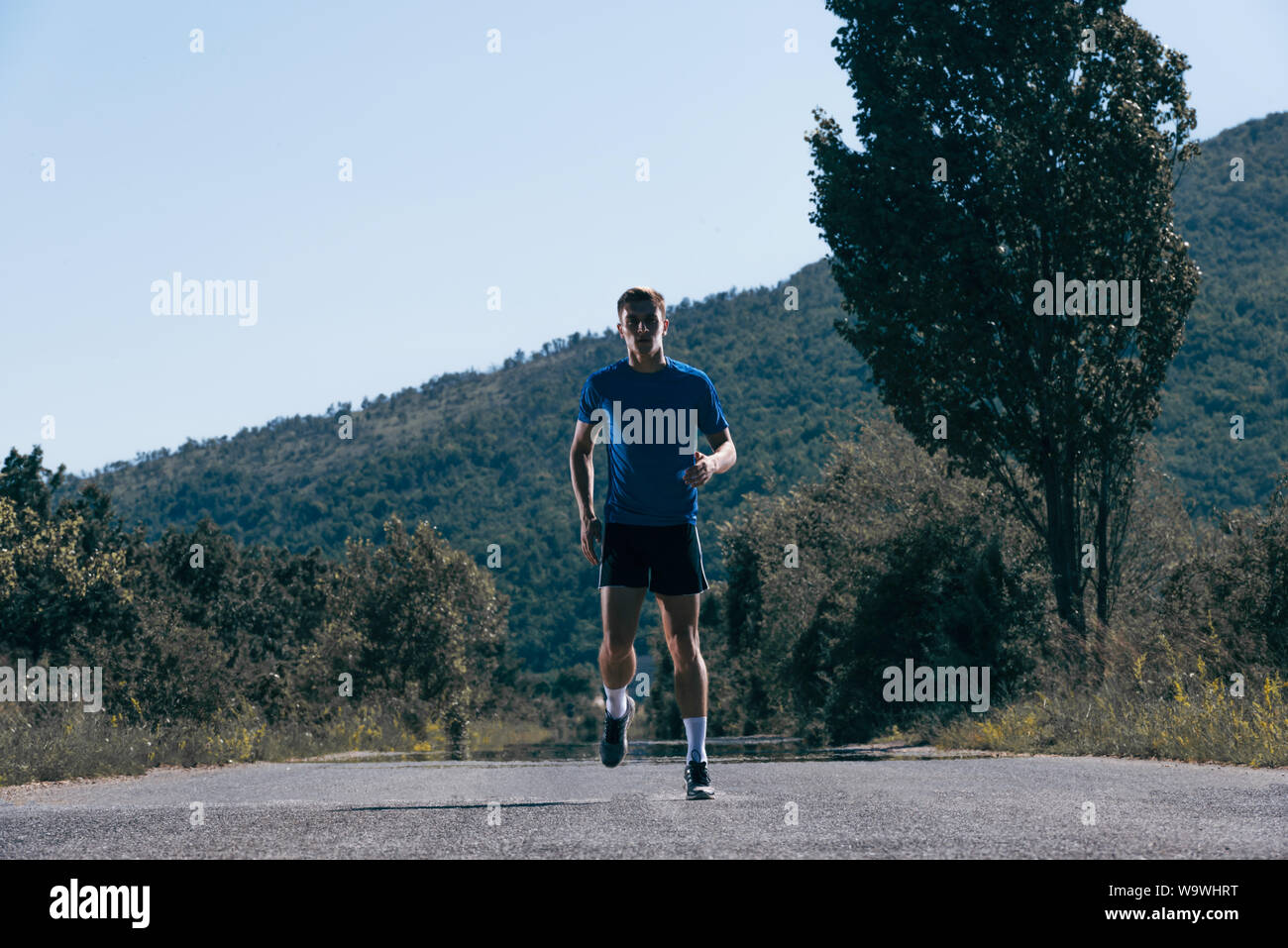 Male athlete running on an empty road in the woods while trying to get ...