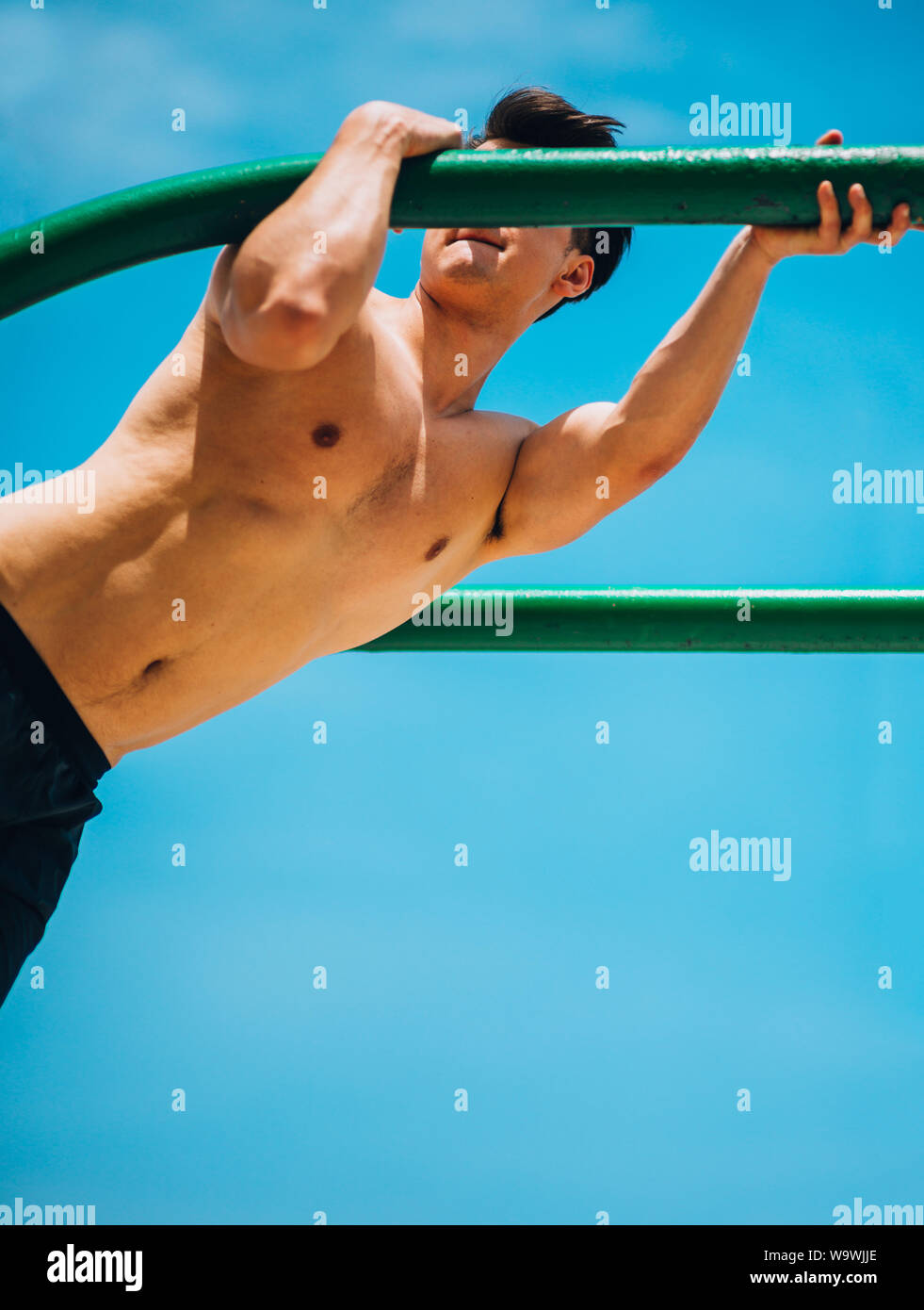 Shirtless guy playing sports on parallel bars,against the blue sky ...