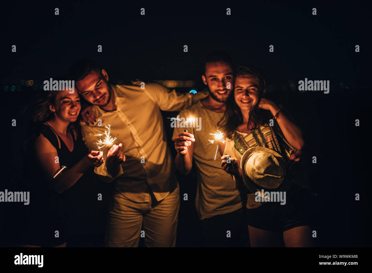 Four young casual friends having fun with sparkling lights in the night ...