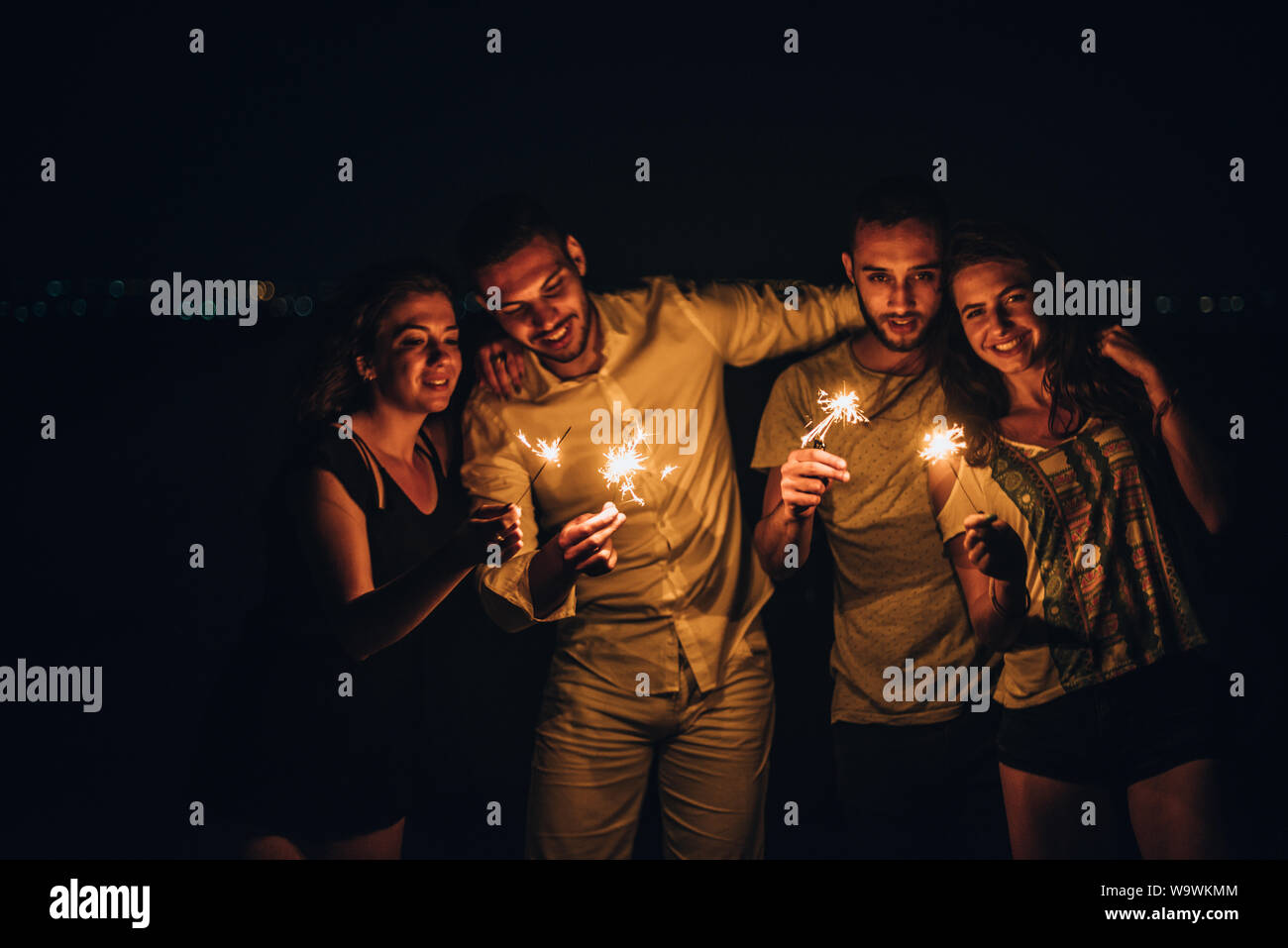 Four young casual friends having fun with sparkling lights in the night ...