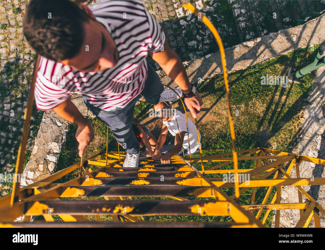 Man going front on high ladder while his two friends are on the bottom ...