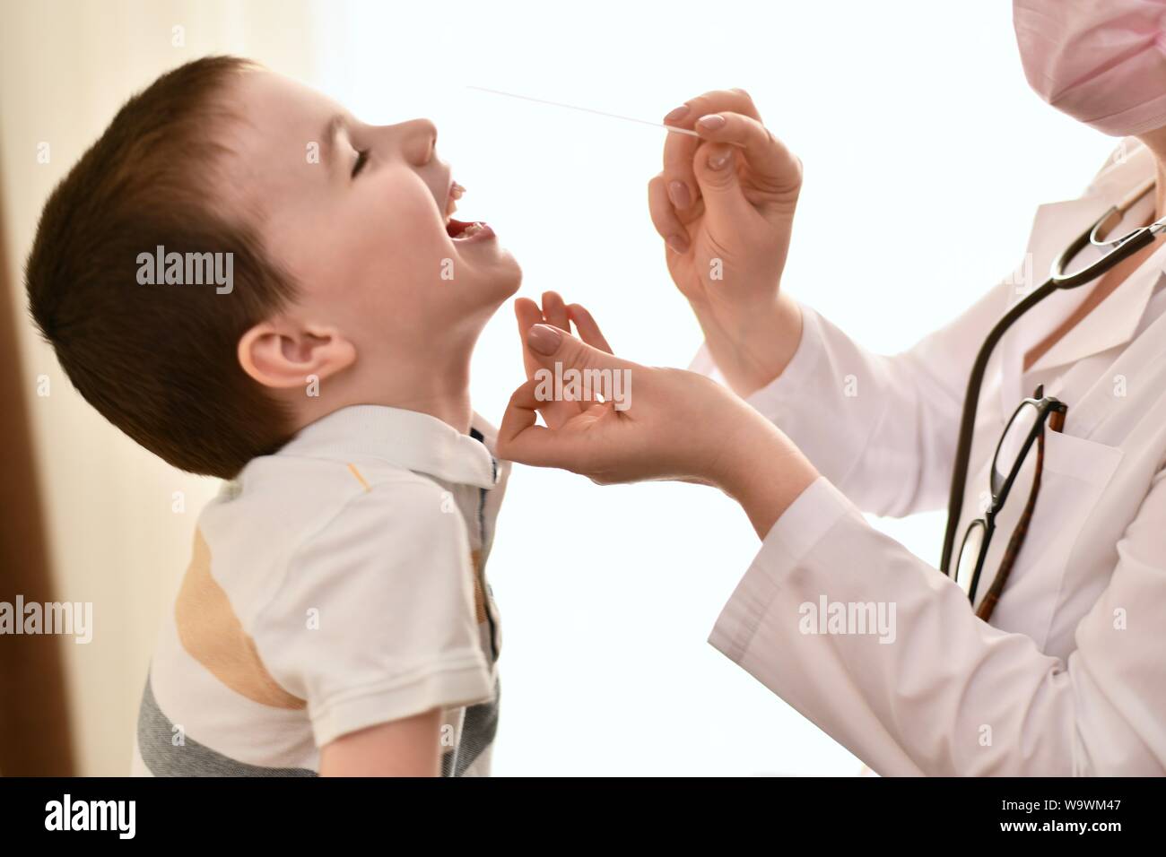 The doctor examines the throat of a child. The boy raised his head ...