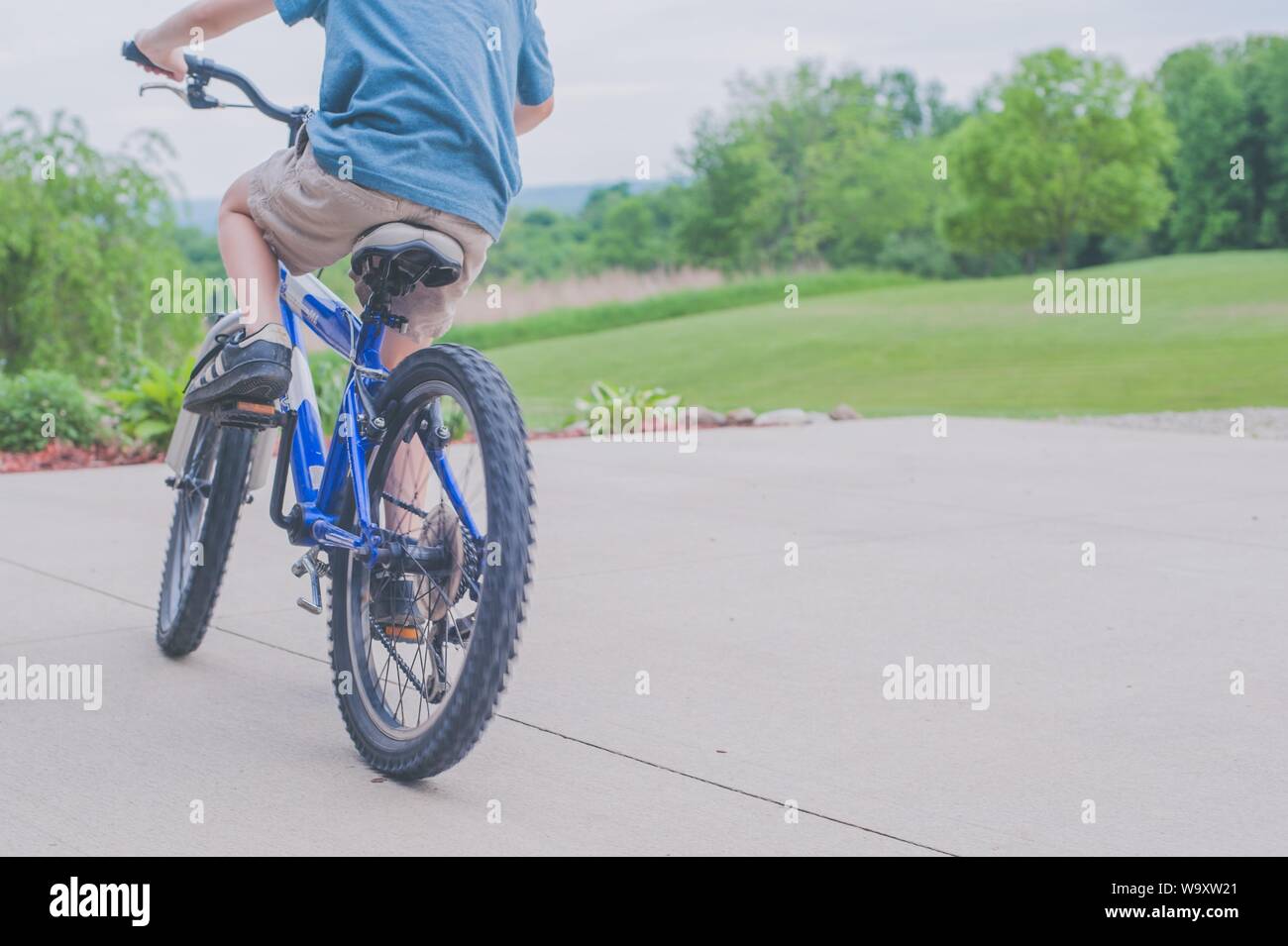 Young boy riding a blue bicycle on gray cement in the countryside Stock ...