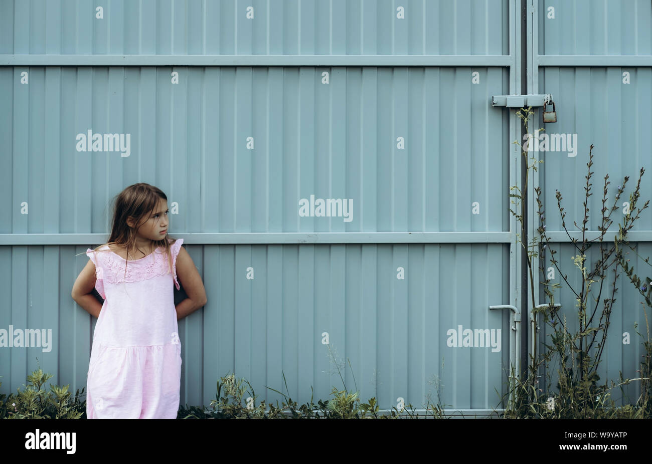 Little serious girl posing near metal gates outdoor. Young beautiful ...