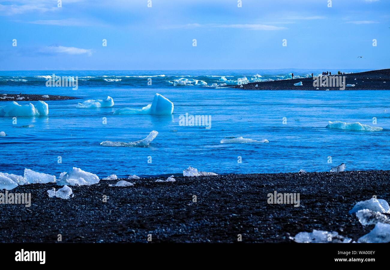 Wide shot of ice cubes on the body of the water beside rocky seashore ...